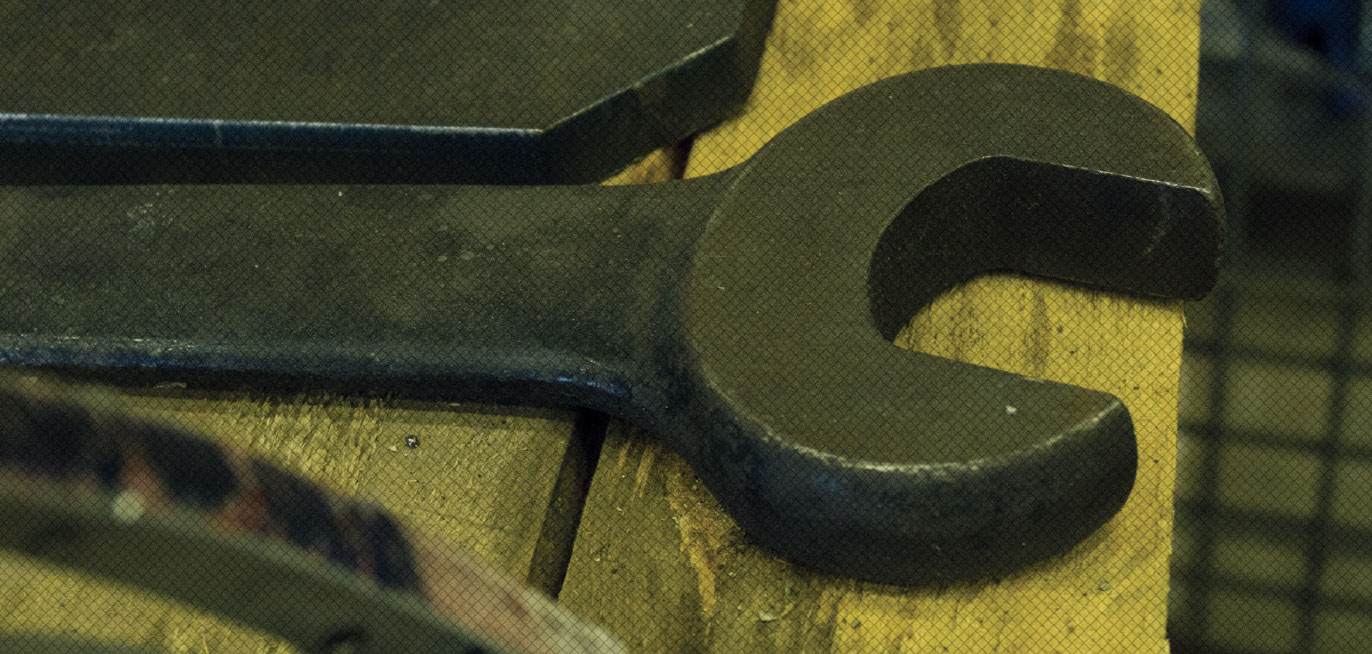 A wrench sits on a wooden work desk. - Helfrich Brothers